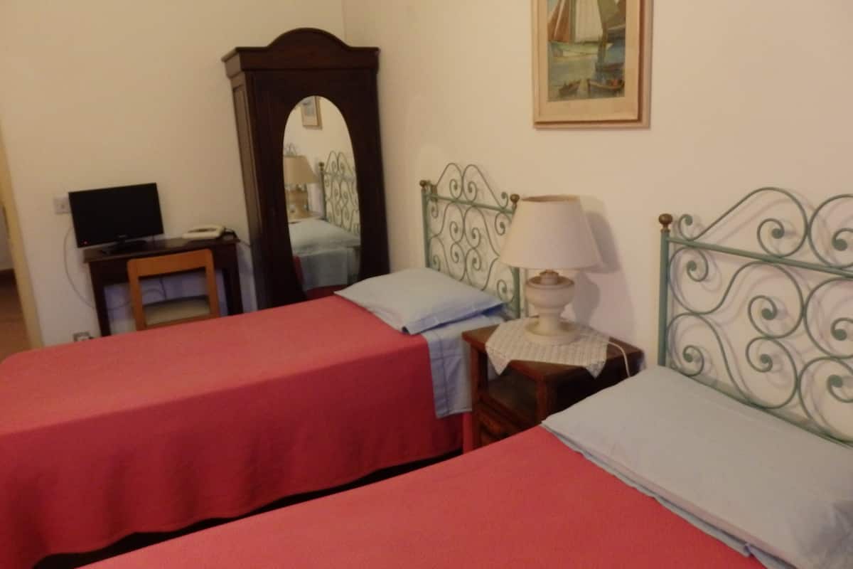 Quarto com duas camas de solteiro, uma escrivaninha com computador, espelho, luminária e um quadro na parede.