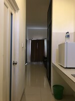 Um corredor estreito com uma porta à esquerda, um refrigerador à direita e uma garrafa de água em cima dele.