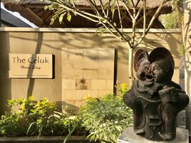 Placa para 'The Celuk Home Stay' numa parede bege, com uma estátua decorativa de um anjo em primeiro plano.