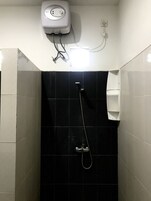 Casa de banho com parede de chuveiro em mosaico preto, aquecedor branco fixado na parede e prateleira branca.