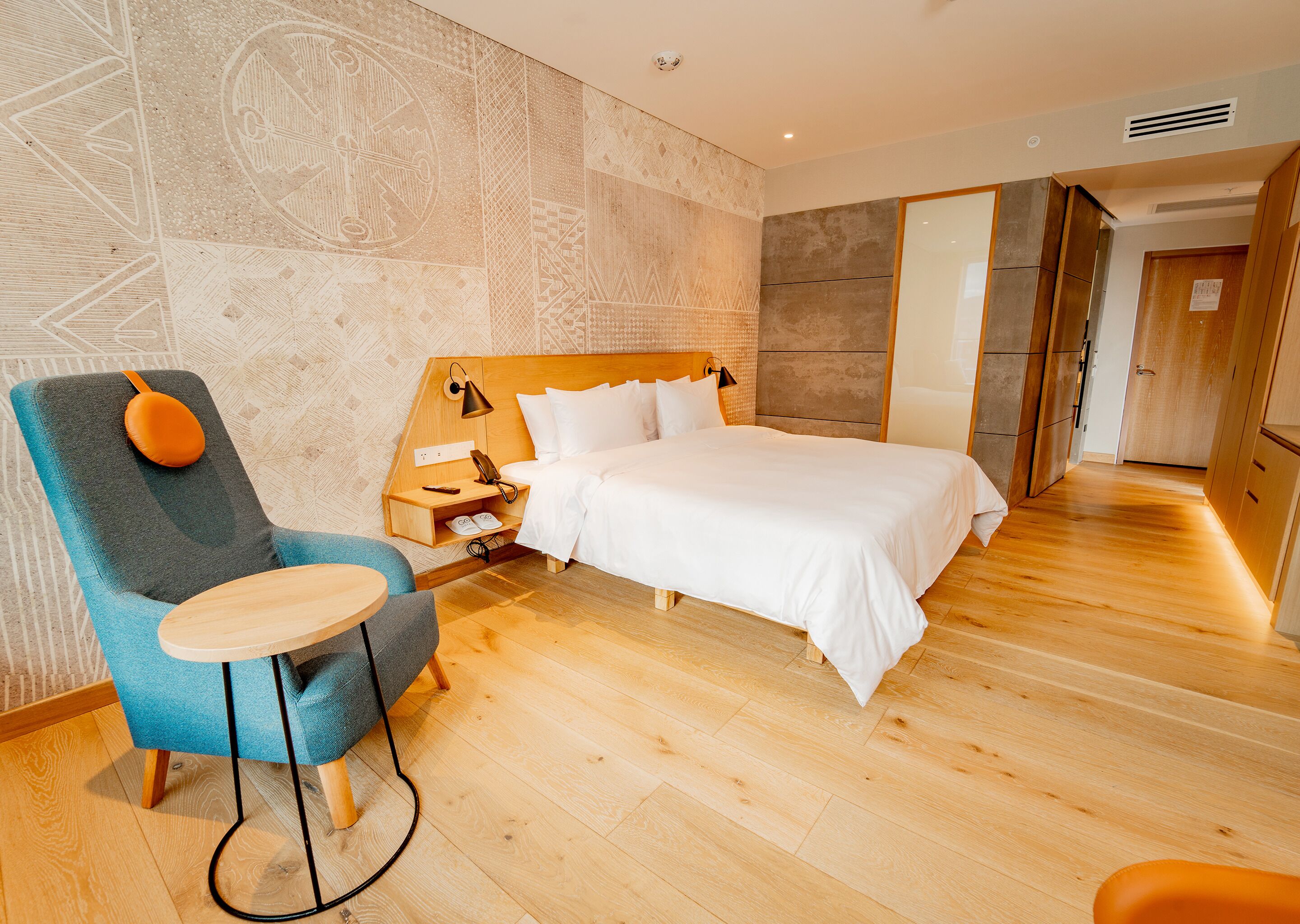 Quarto de hotel moderno com uma cama grande, uma mesinha de cabeceira, uma cadeira e uma pequena mesa.