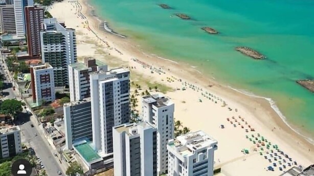 Paisagem costeira com edifícios altos, uma praia de areia e águas turquesa cristalinas.