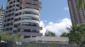Um hotel alto e moderno com fachada curva, várias varandas e área de piscina com palmeiras.