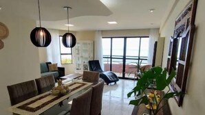 Uma área de refeições moderna com uma mesa longa, cadeiras, lumin árias pendentes e um vaso de planta.