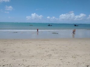 Uma praia com céu claro, águas calmas e alguns barcos.