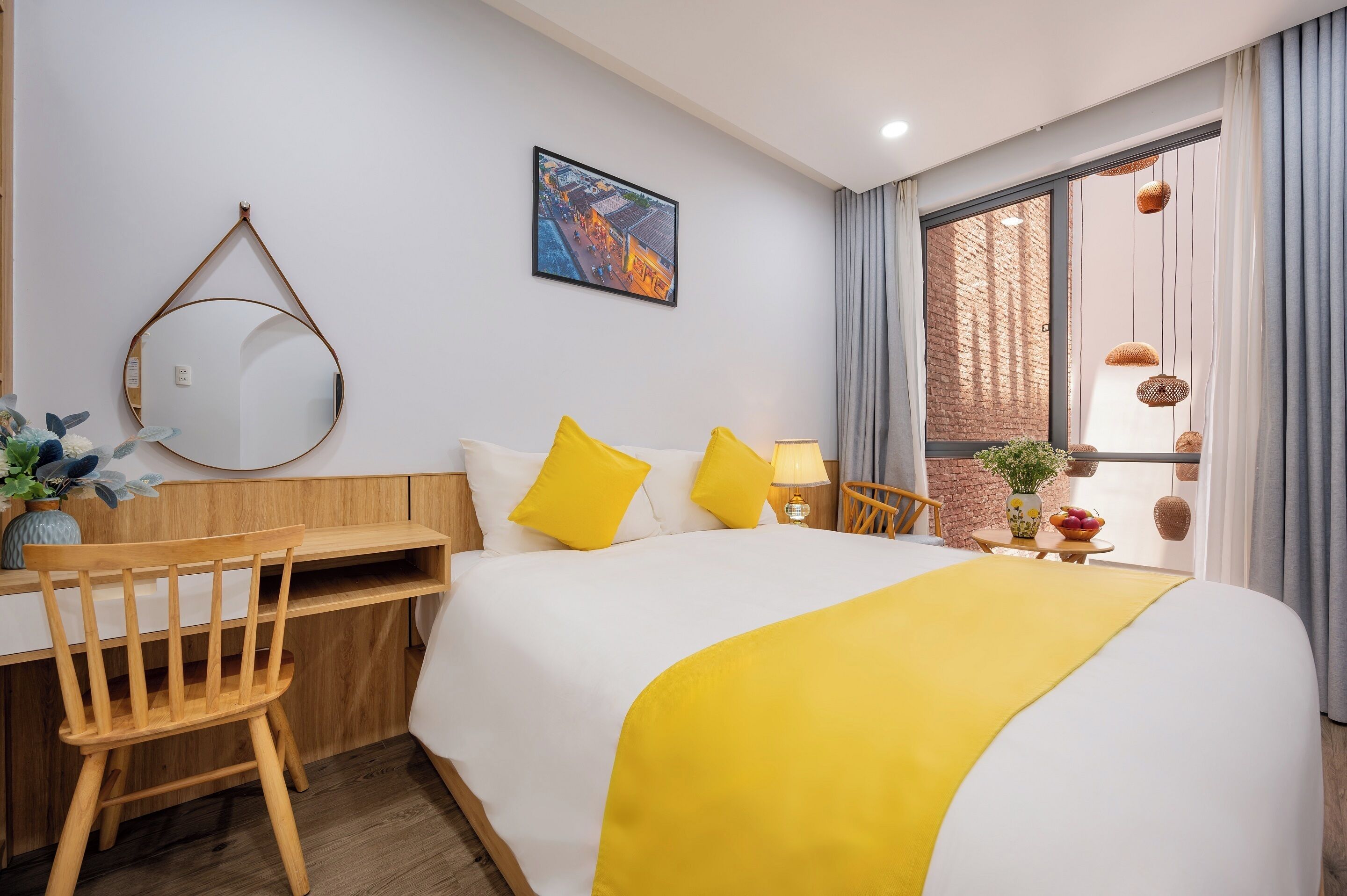Quarto de hotel com cama, escrivaninha, cadeira, uma janela grande e luminária pendente.