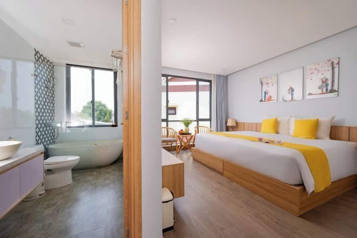 Quarto de hotel moderno com cama grande, banheiro, área de refeições e janelas amplas.