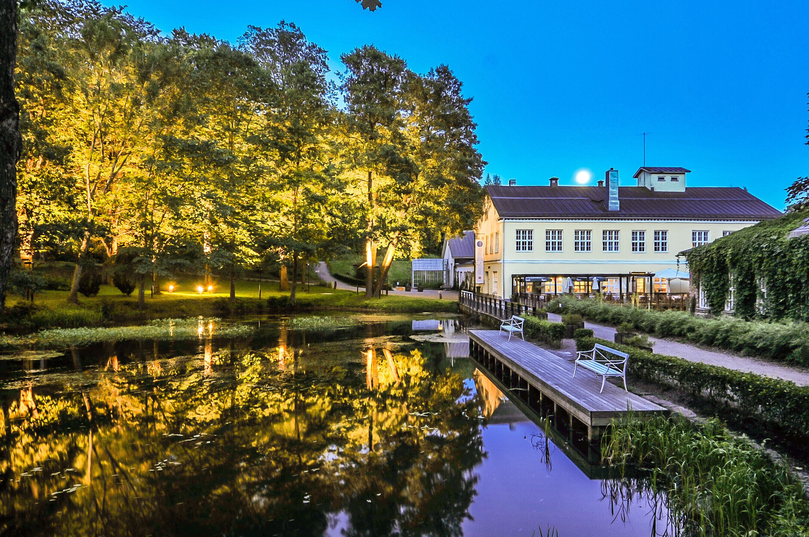 Hotel na beira do lago com um cais, reflexo de árvores e um jardim bem cuidado.