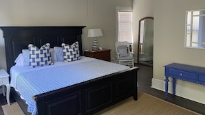 Quarto com uma cama grande, mesa de cabeceira, cadeira, cômoda e espelho.