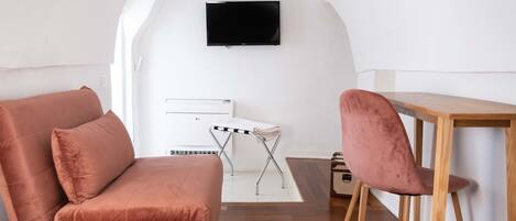 Uma sala de estar moderna com um sofá rosa, uma mesa de madeira e uma TV fixada na parede.