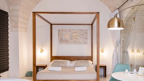 Uma cama de dossel com estrutura de madeira, uma pintura abstrata grande acima dela e uma mesa redonda com cadeiras em primeiro plano.