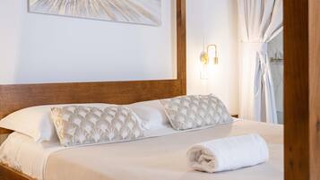 Cama bem arrumada com lençóis brancos e almofadas estampadas, cabeceira de madeira, luminária fixada na parede e uma obra de arte abstrata emoldurada acima da cama.