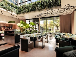 Um restaurante moderno com plantas, mesas redondas e assentos confortáveis.