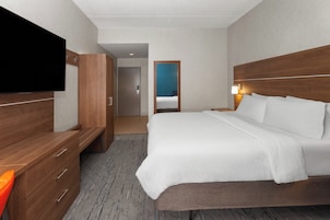 Quarto de hotel com uma cama, televisão, secretária e guarda-roupa.