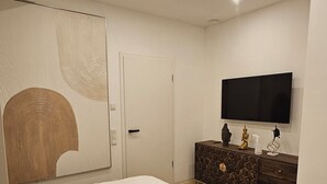 Quarto moderno com uma cama grande, penteadeira, TV de tela plana e luminária no teto.