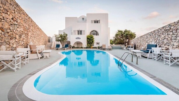 Piscina com espreguiçadeiras e um muro de pedra.