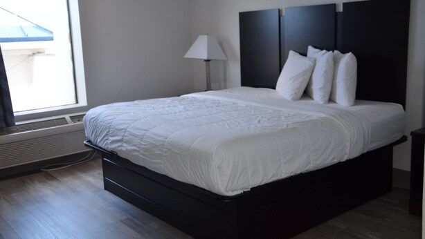 Quarto de hotel moderno com uma cama grande, mesa de cabeceira, abajur e janela com persianas.