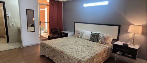 Quarto de hotel com cama, mesas de cabeceira, espelho, abajur e vista para o exterior.