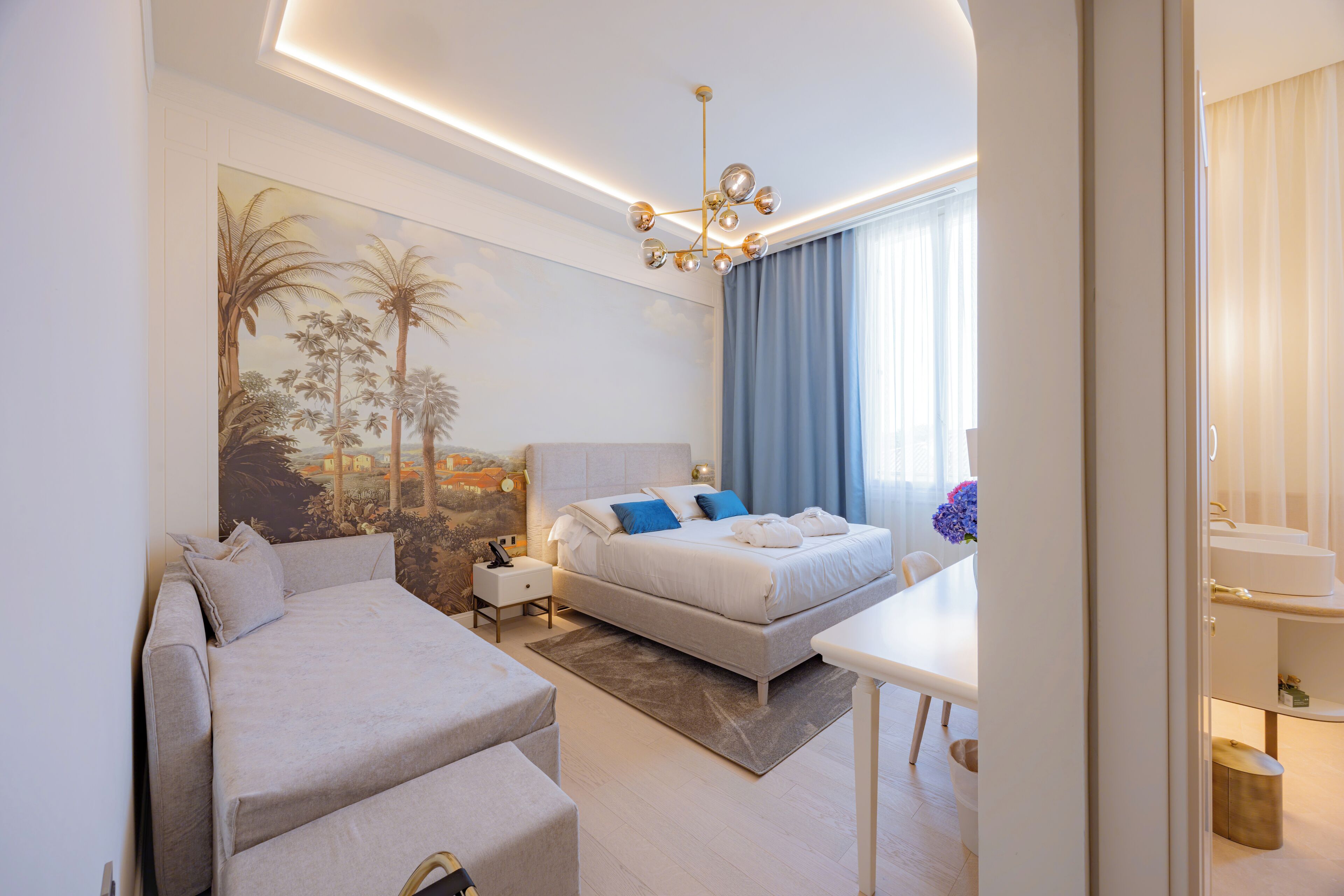 Quarto de hotel moderno com cama, sofá, mesa de jantar e um quadro na parede.