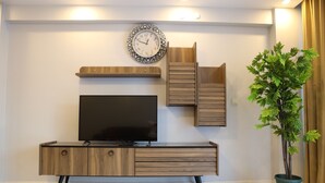 Uma sala de estar moderna com televisão de tela plana, armários de madeira, um relógio decorativo e um vaso com planta.