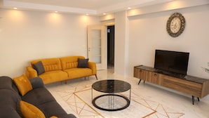 Uma sala de estar moderna com um sofá seccional, uma mesa de centro e uma TV sobre um móvel de madeira.