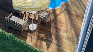 Um deck de madeira com piscina, espreguiçadeiras e um guarda-sol.