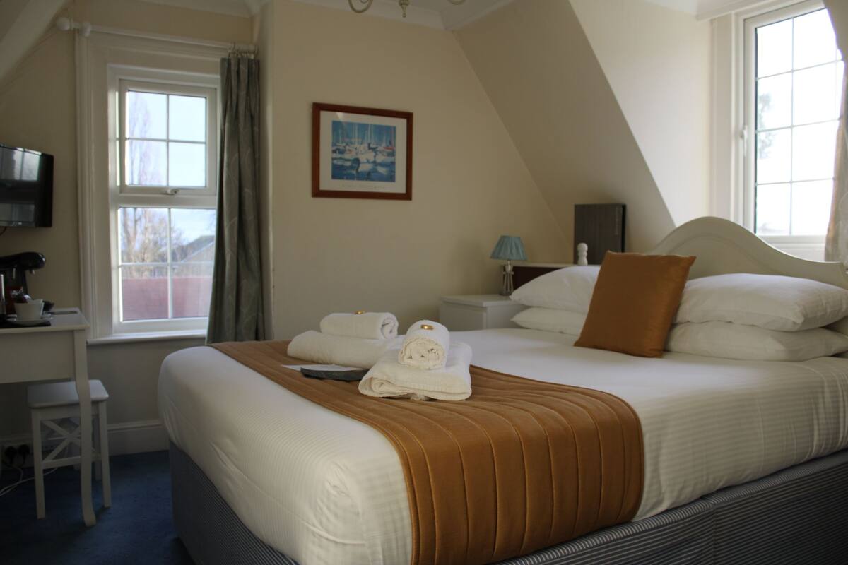 Quarto de hotel com uma cama grande, uma escrivaninha, uma cadeira, uma televisão e uma janela com cortinas.