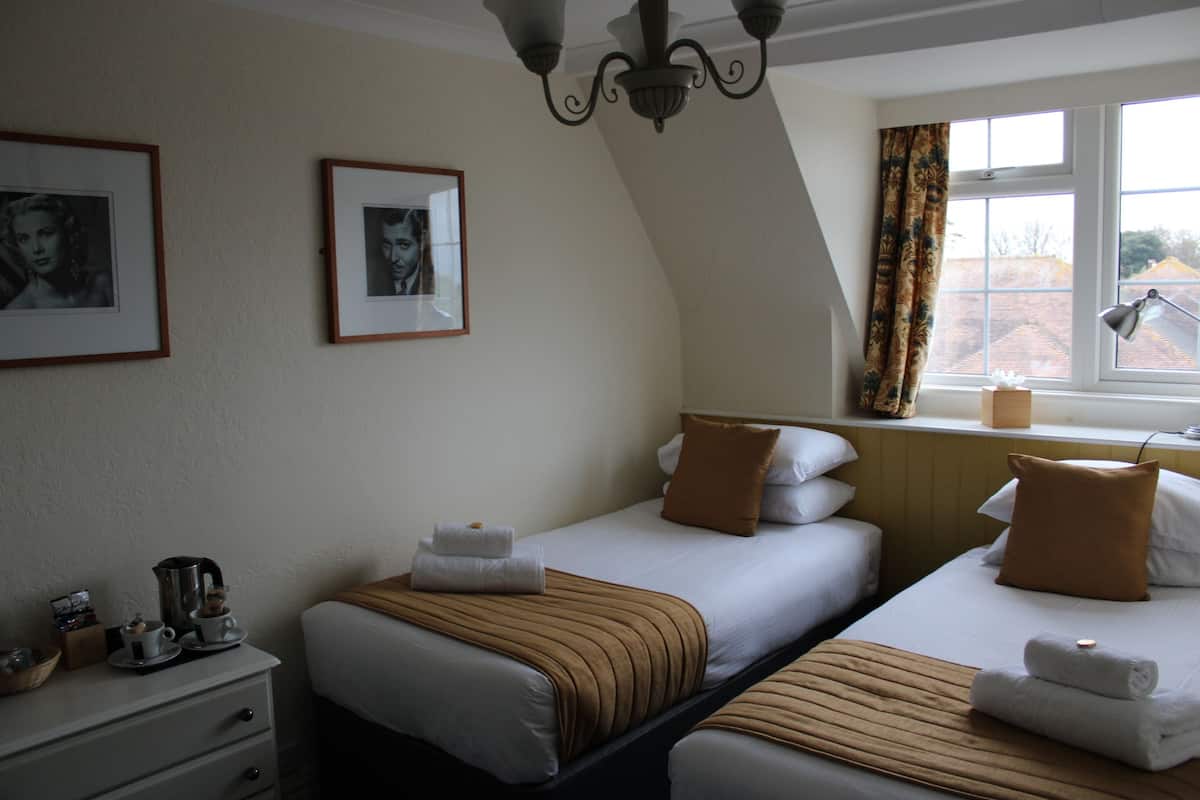 Quarto de hotel com duas camas, uma mesa de escritório com cafeteira, quadros nas paredes e uma janela com cortinas.