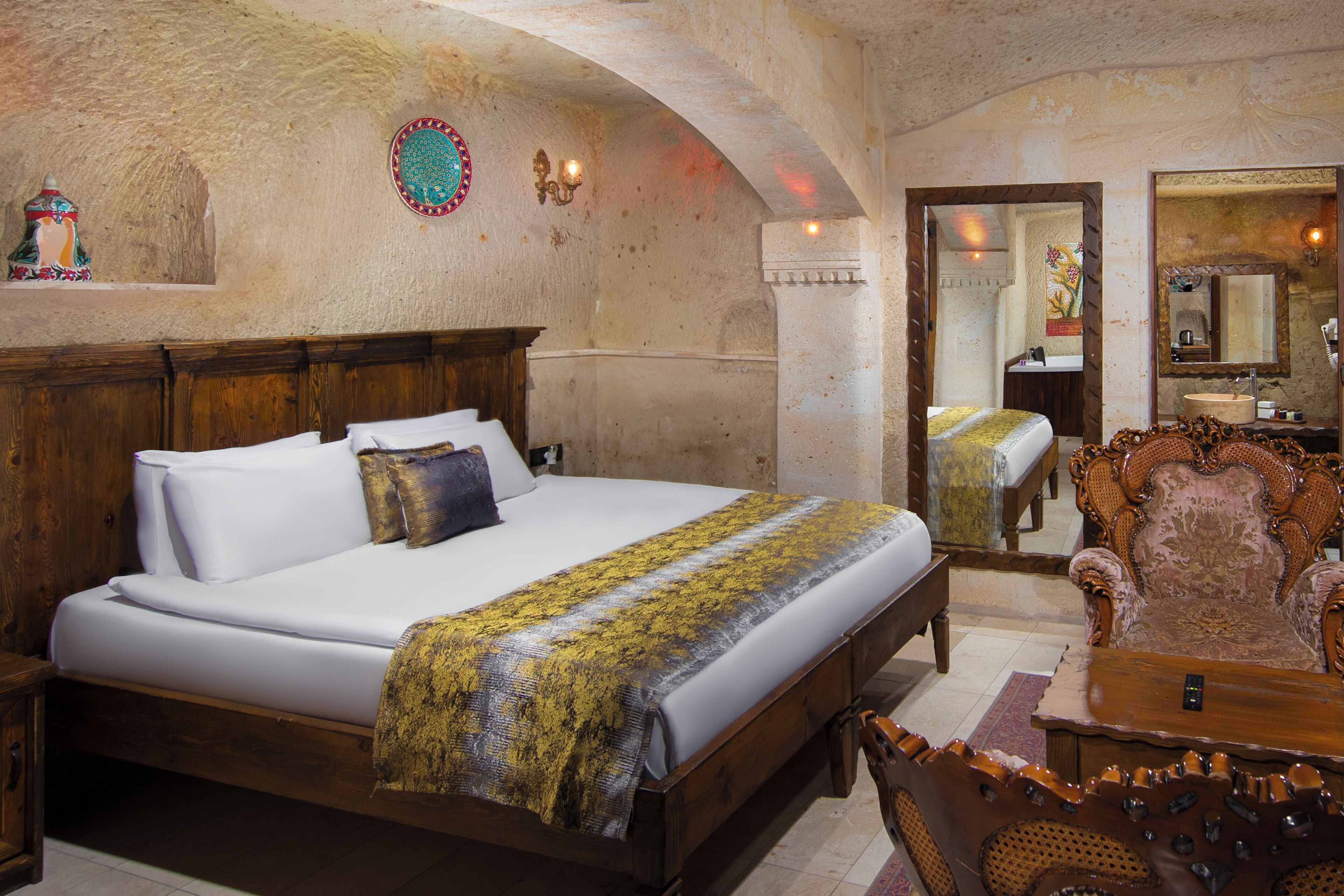 Quarto com uma cama grande, cabeceira de madeira, um espelho e uma cadeira de madeira.