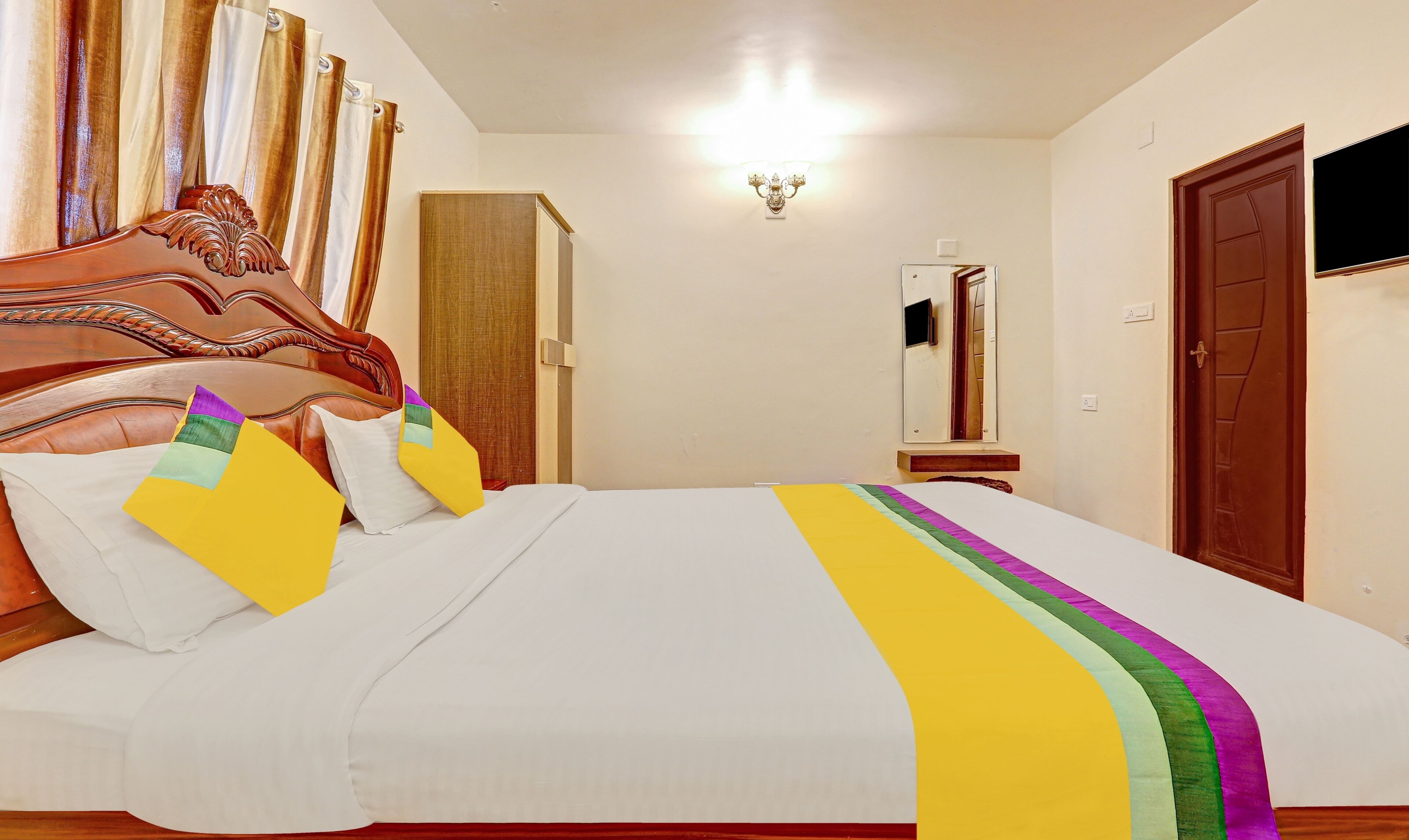 Quarto de hotel com uma cama grande, cabeceira de madeira, espelho e porta.