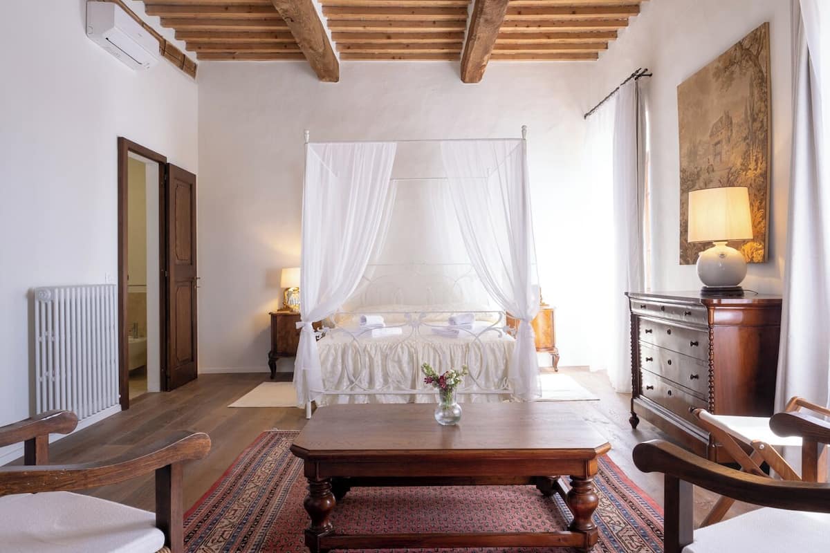 Quarto com uma cama de dossel, uma mesa de madeira, cômoda e radiador.