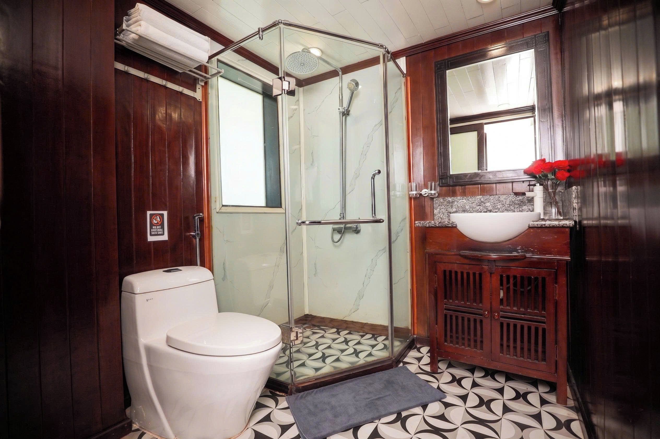 Casa de banho com cabine de chuveiro de vidro, sanita branca e toucador de madeira com lavatório.