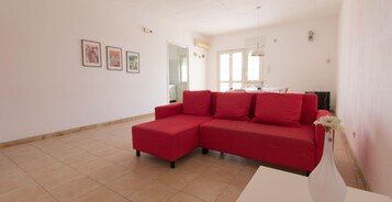 Uma sala de estar ampla com um sofá seccional vermelho, uma mesa de centro branca e um vaso com flores.