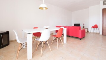 Uma sala de estar moderna com uma mesa de jantar branca, cadeiras vermelhas e brancas, um sofá vermelho e uma televisão.