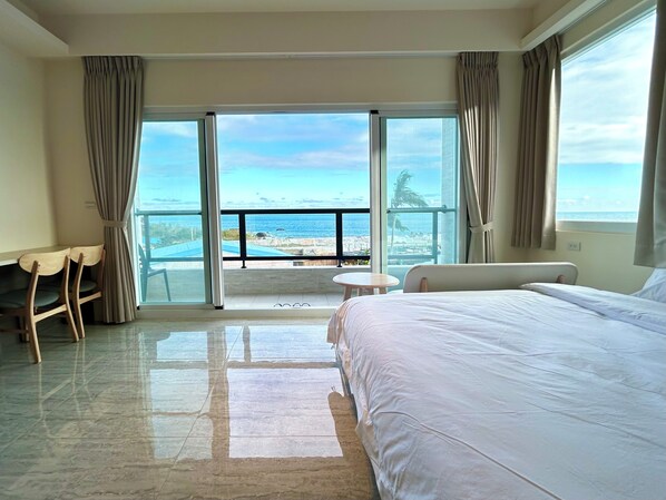 Quarto de hotel com uma cama grande, uma escrivaninha e vista para a praia.