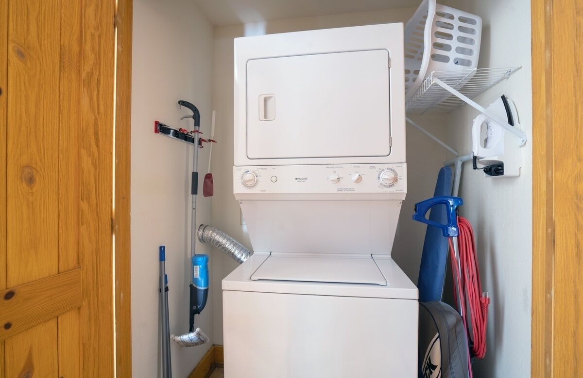 Uma lavanderia compacta com máquina de lavar e secar frontal, um varal e uma mangueira para água.