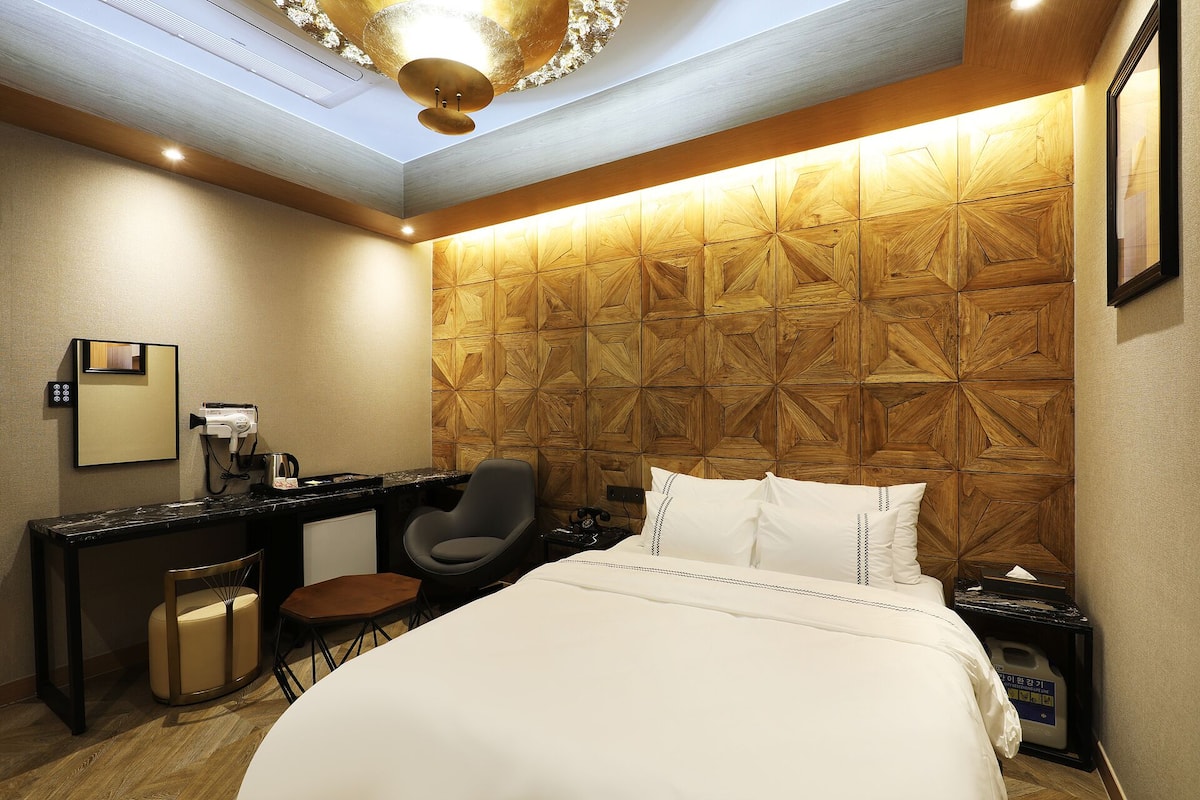 Quarto de hotel com uma cama grande, uma escrivaninha, uma cadeira, uma máquina de café e uma parede com padrão geométrico.