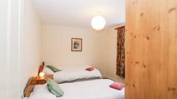 Um quarto pequeno e acolhedor com duas camas de solteiro, uma mesa de cabeceira com abajur, um quadro na parede e uma porta de madeira.