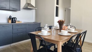 Cozinha moderna com armários escuros, exaustor de aço inoxidável e área de jantar com mesa de madeira posta para quatro pessoas.