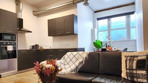 Cozinha moderna com armários escuros, micro-ondas e fogão. Há uma área de jantar com um sofá de couro preto e uma mesa com um vaso de flores.