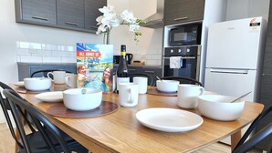 Uma cozinha moderna com uma mesa de jantar de madeira posta com tigelas e pratos brancos, uma garrafa de vinho e uma revista.