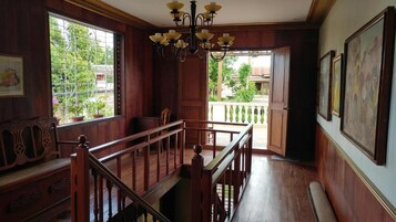 Interior em madeira com escadaria, um candelabro e varanda com vista para o verde.