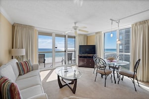 Quarto de hotel com varanda, sofá, mesa de jantar e televisão.