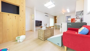 Uma sala de estar moderna com um sofá vermelho, um painel de madeira, uma televisão e um espaço de jantar com mesa e cadeiras.