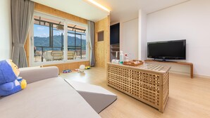 Uma sala de estar moderna com um sofá, uma TV e vista para montanhas através de grandes janelas.