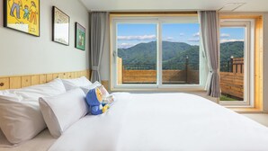 Quarto de hotel com uma cama grande, uma janela com vista para uma montanha arborizada e obras de arte na parede.