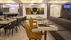 Uma sala de jantar moderna com uma mesa comprida, assentos confortáveis e uma grande pintura na parede.