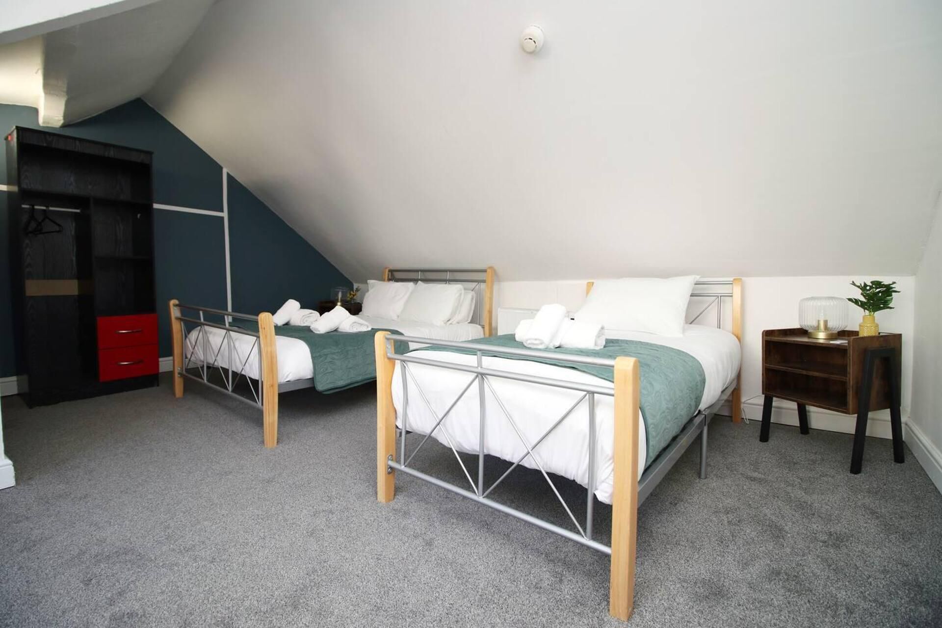 Quarto com duas camas, um guarda-roupa e uma mesa de cabeceira com luminária.
