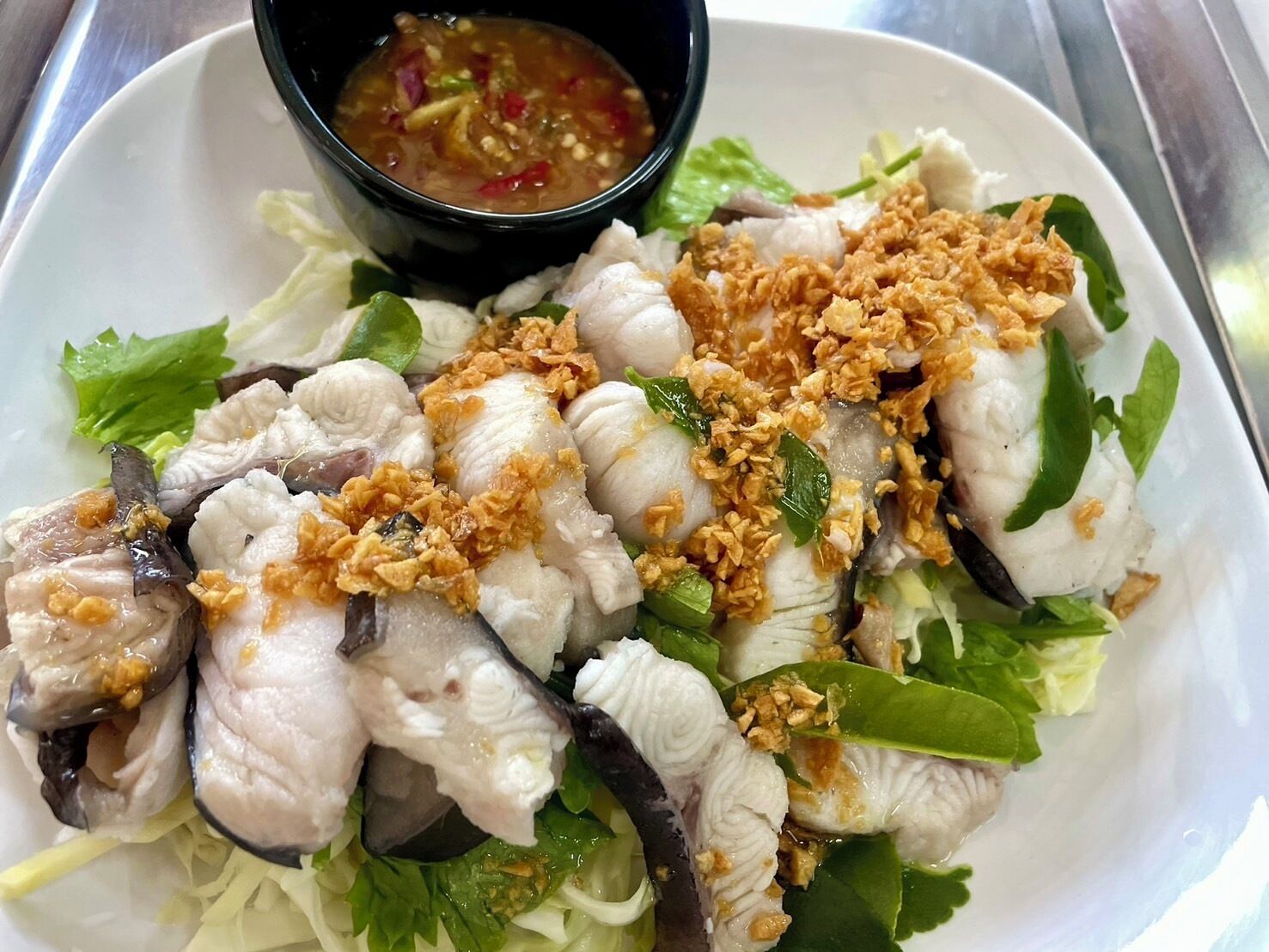Uma salada de peixe com cebolas fritas crocantes e um acompanhamento de molho para mergulhar.