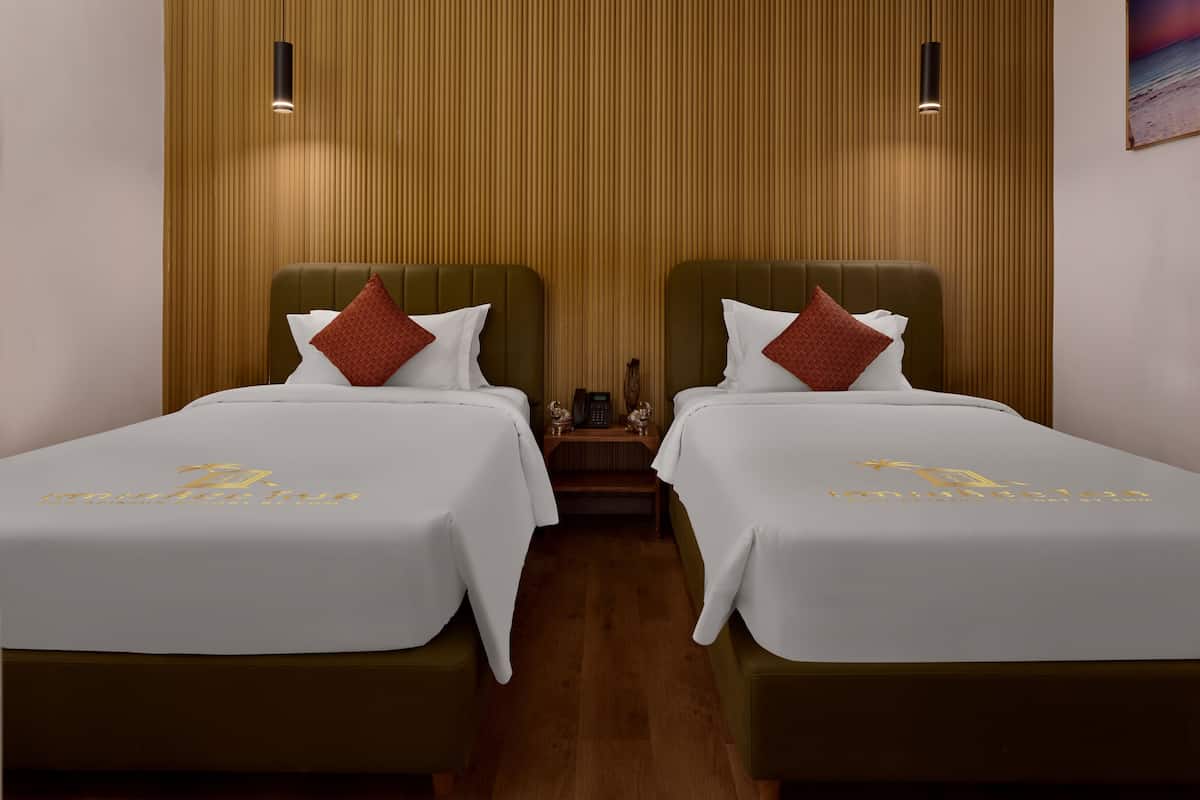 Quarto de hotel com duas camas, cada uma com colcha branca e emblema dourado. O quarto possui painéis de madeira nas paredes e uma pequena mesa de cabeceira entre as camas.